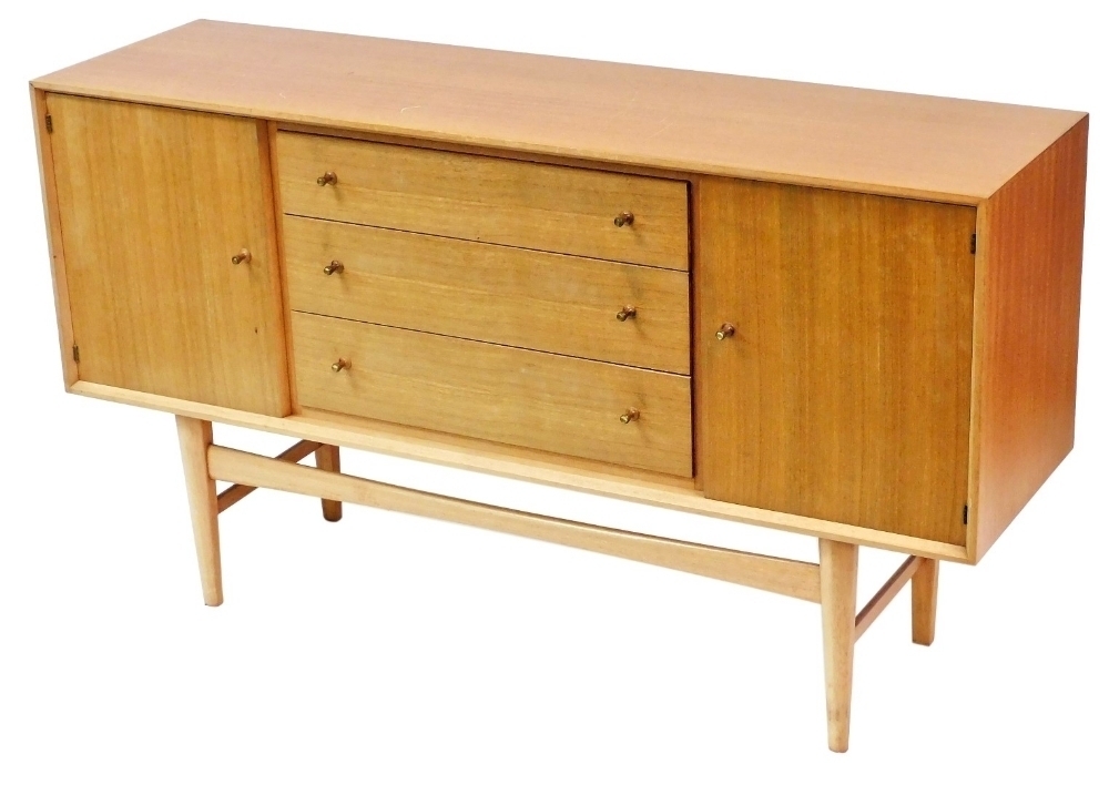 A 1950s teak sideboard, with three long drawers, flanked by a pair of ...