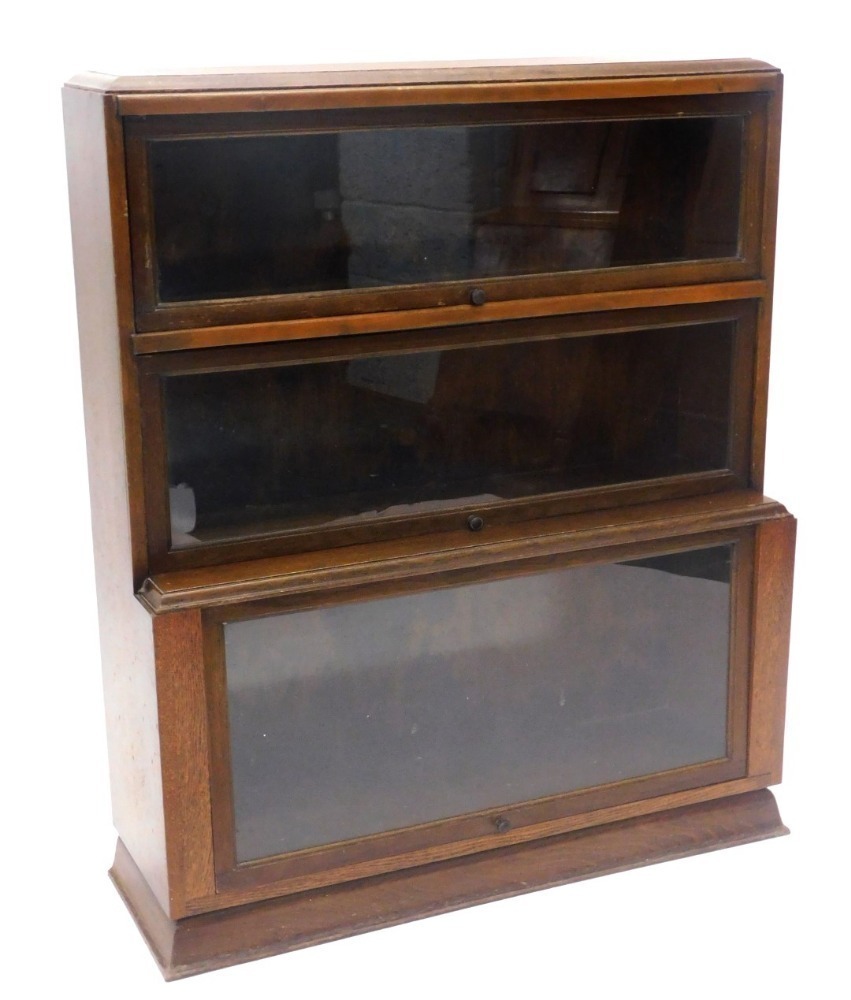 An oak bookcase, with three hinged glazed sliding doors, on a plinth ...