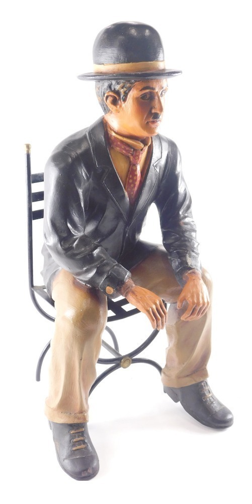 A painted composition figure of a seated Charlie Chaplin, with chair ...