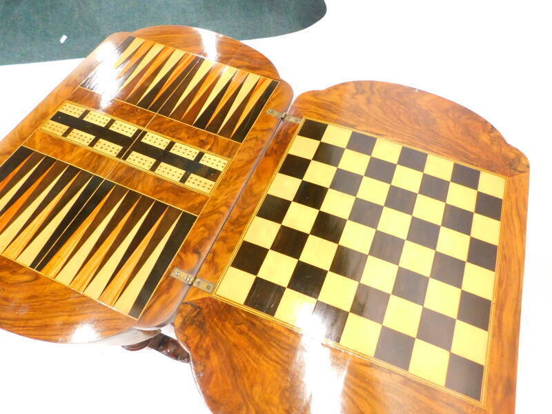 A Victorian burr walnut games/ work table, the hinged shaped top with a ...