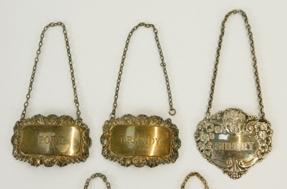 Five decanter labels, comprising three silver labels, one with cherub ...