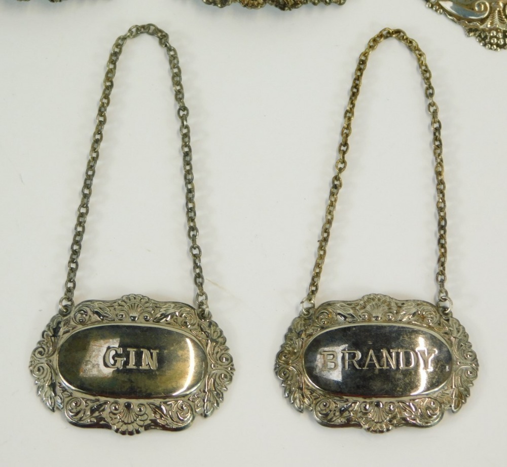 Five decanter labels, comprising three silver labels, one with cherub ...