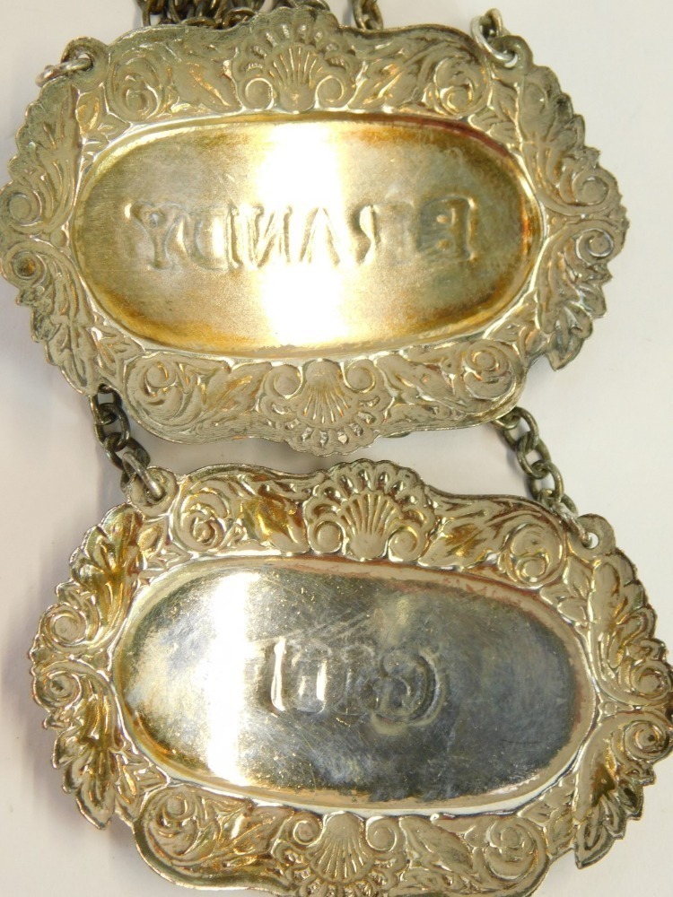Five decanter labels, comprising three silver labels, one with cherub ...